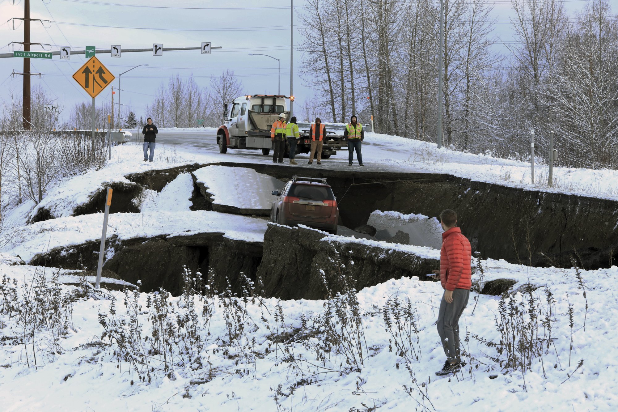 "Highway workers and spectators look at a car stuck on a section of an ...